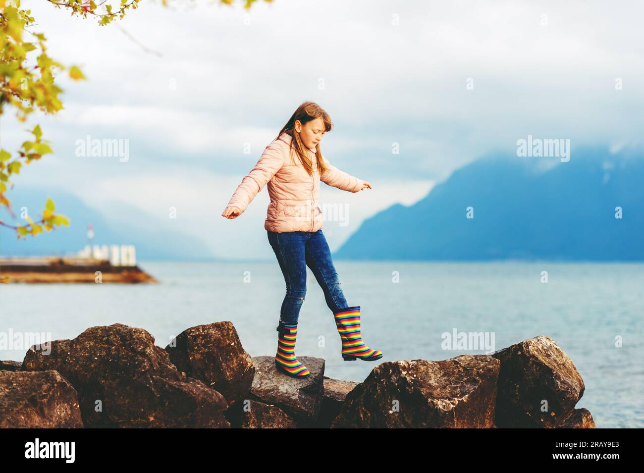 Adorable kid girl playing by the lake on a very cloudy day, wearing ...