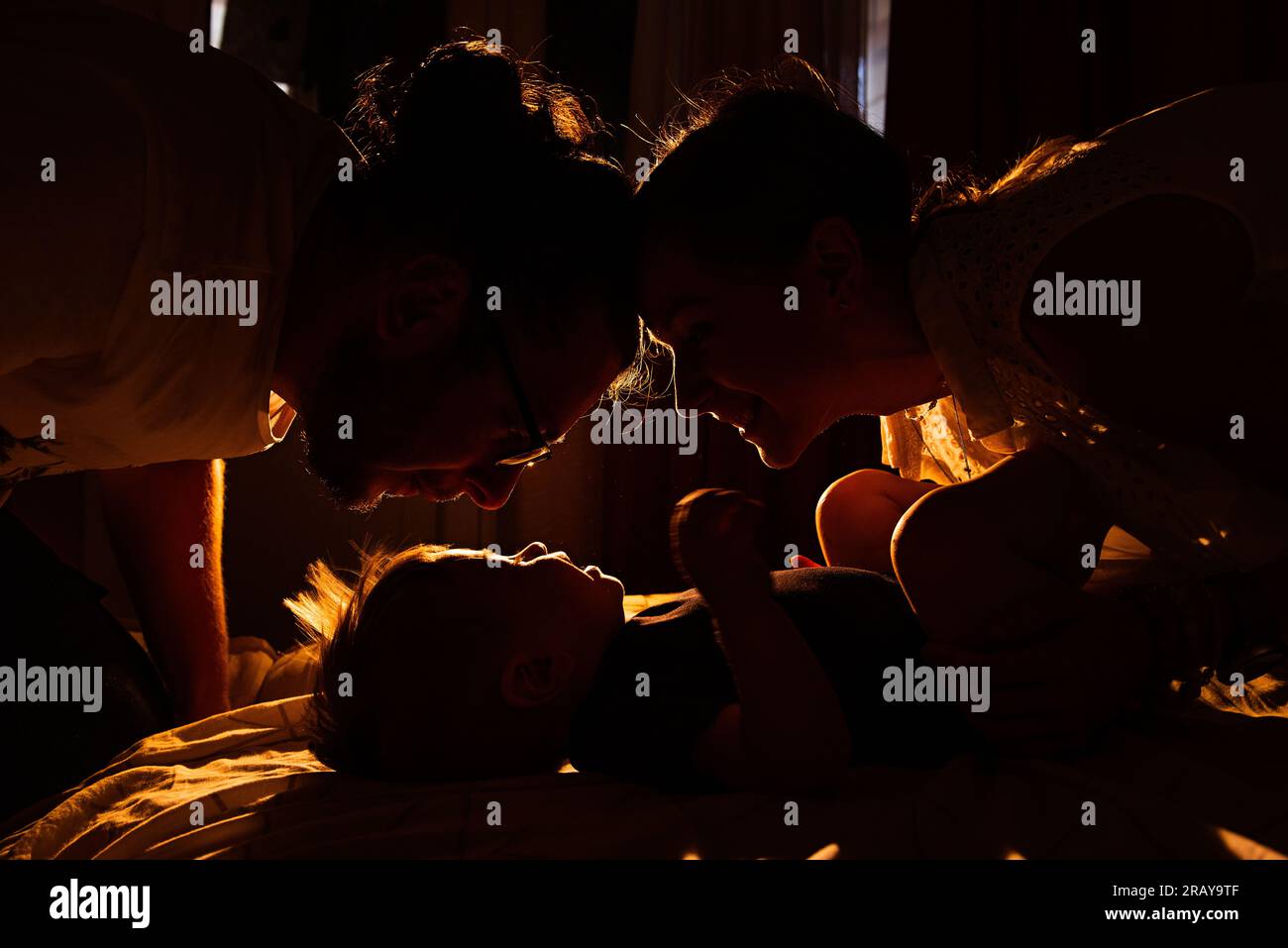 Dark silhouette of mother and father, who leaned over baby at night ...