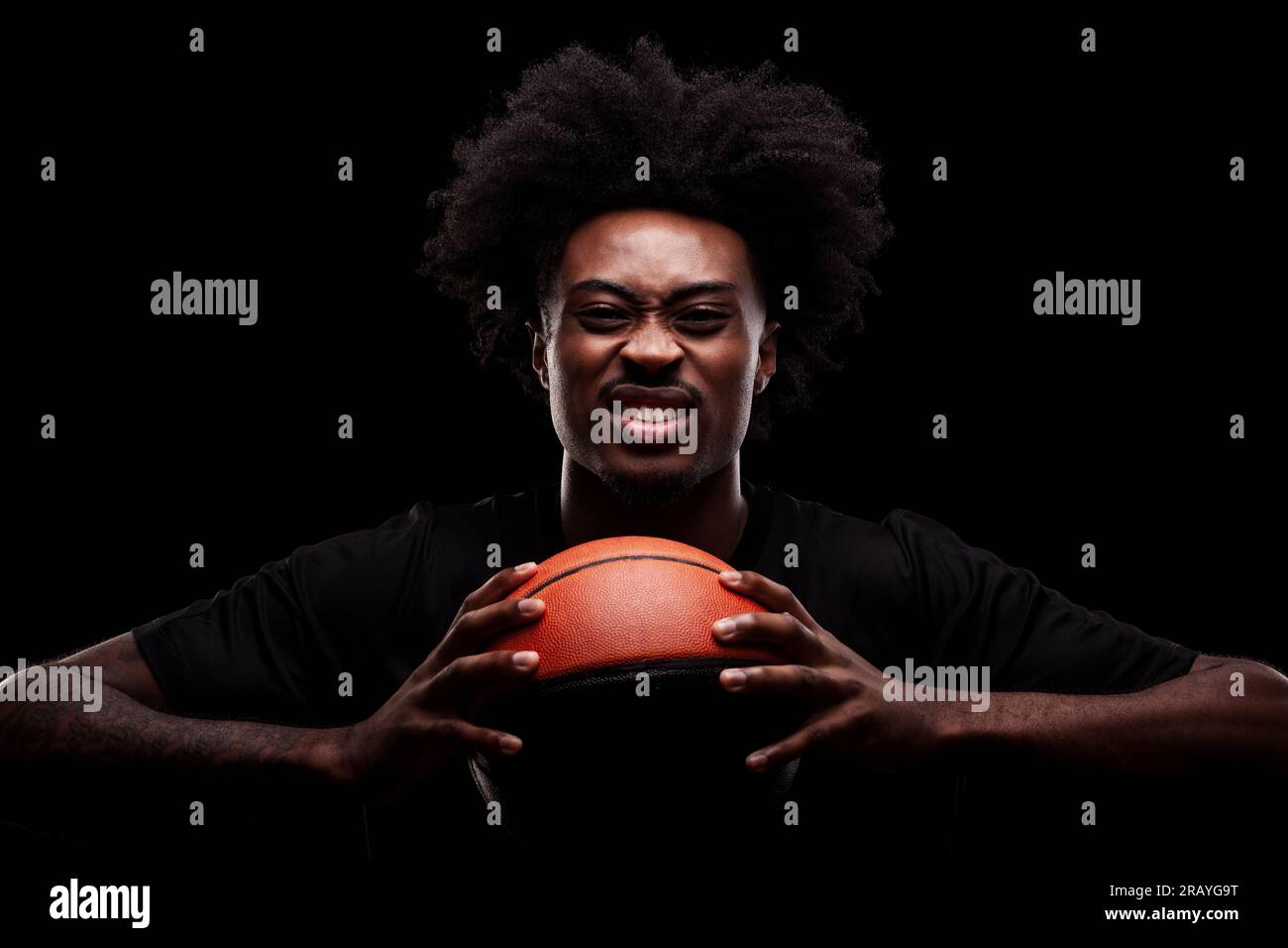 Basketball player holding a ball against black background and screaming ...