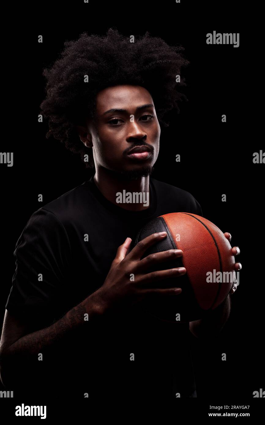 Basketball player holding a ball against black background. Serious ...