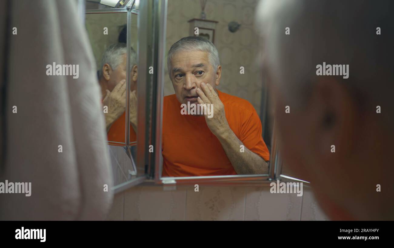 Senior man grooming himself in front of mirror during morning ritual ...