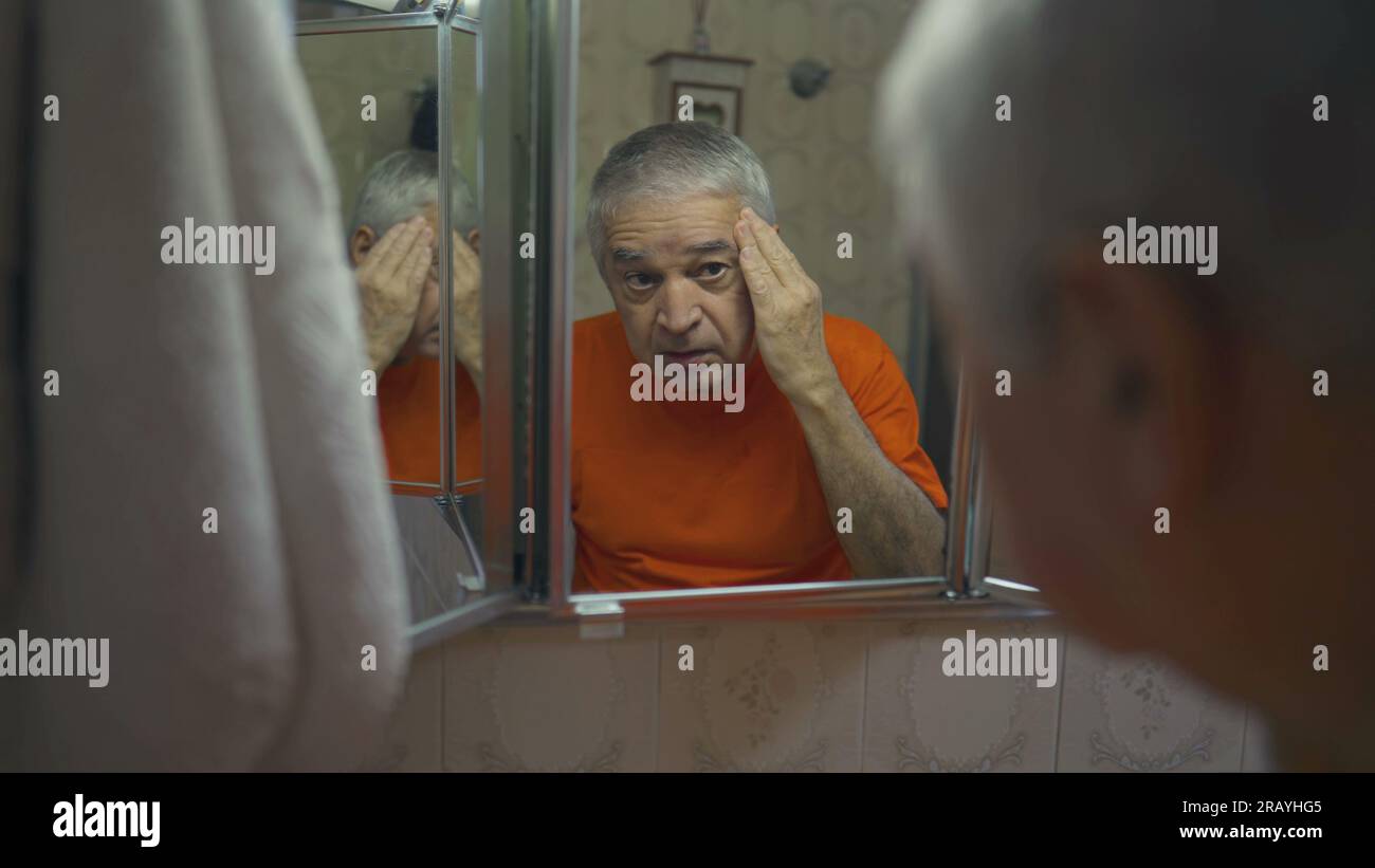Senior man grooming himself in front of mirror during morning ritual ...