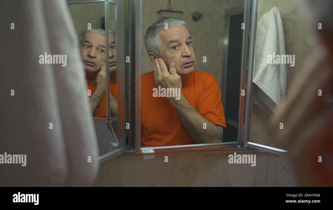 Senior man grooming himself in front of mirror during morning ritual ...