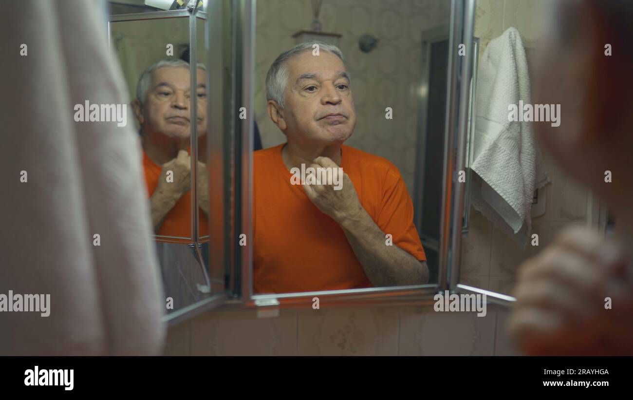 Senior man grooming himself in front of mirror during morning ritual ...