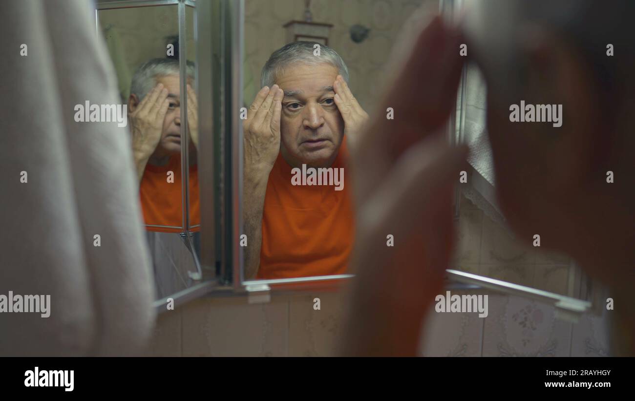 Senior man grooming himself in front of mirror during morning ritual ...
