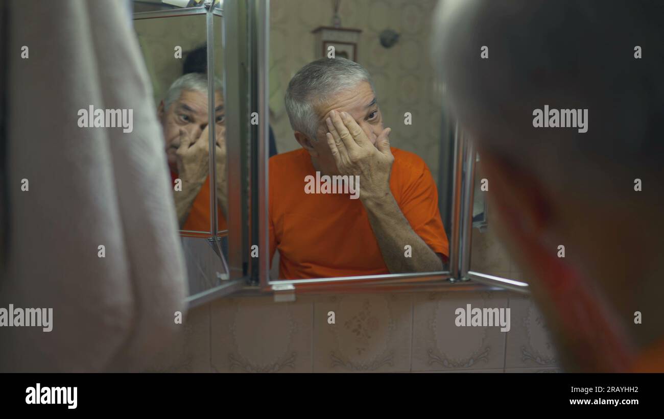 Senior man grooming himself in front of mirror during morning ritual ...