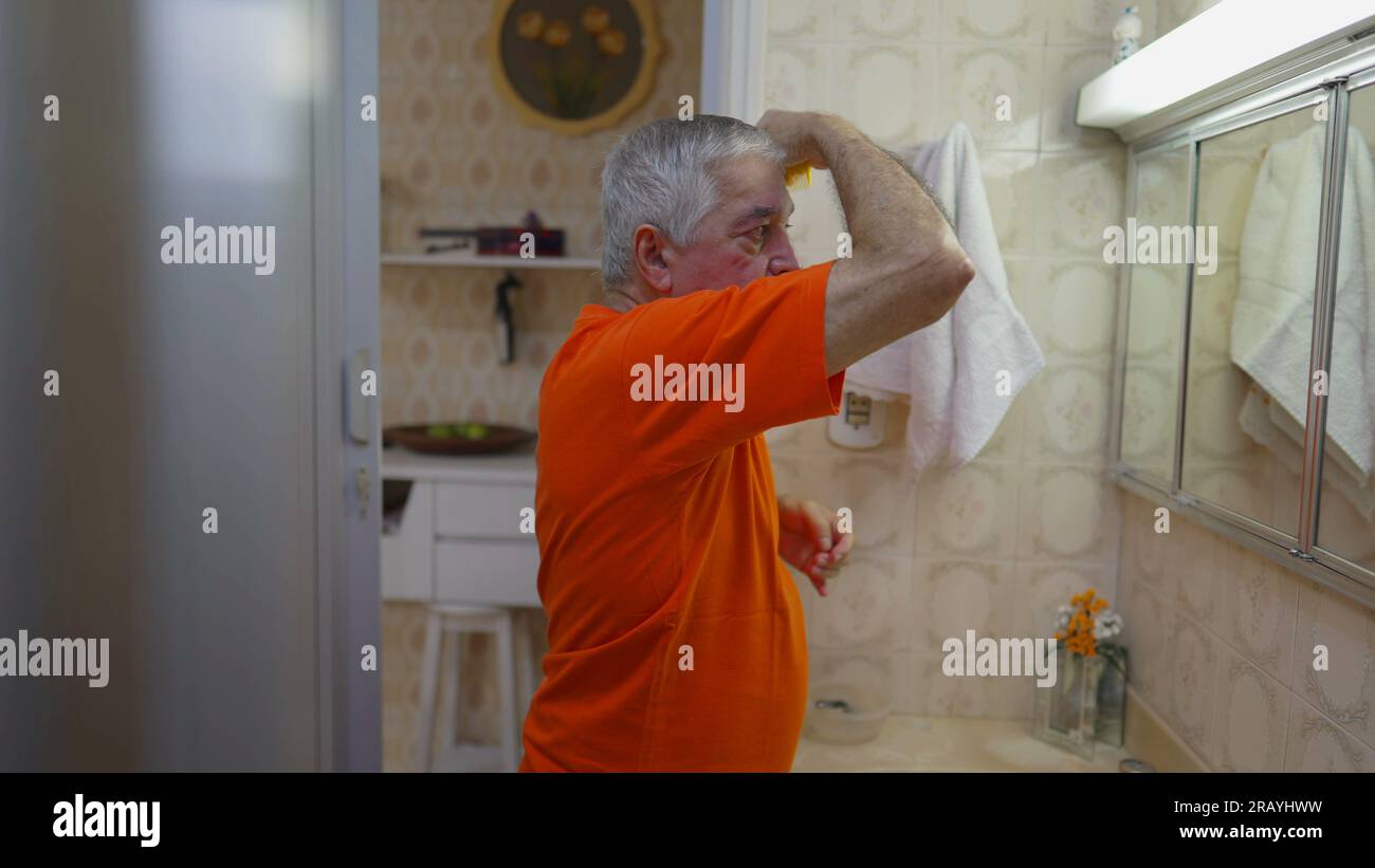 Senior man combing hair in front of bathroom mirror, domestic old age ...