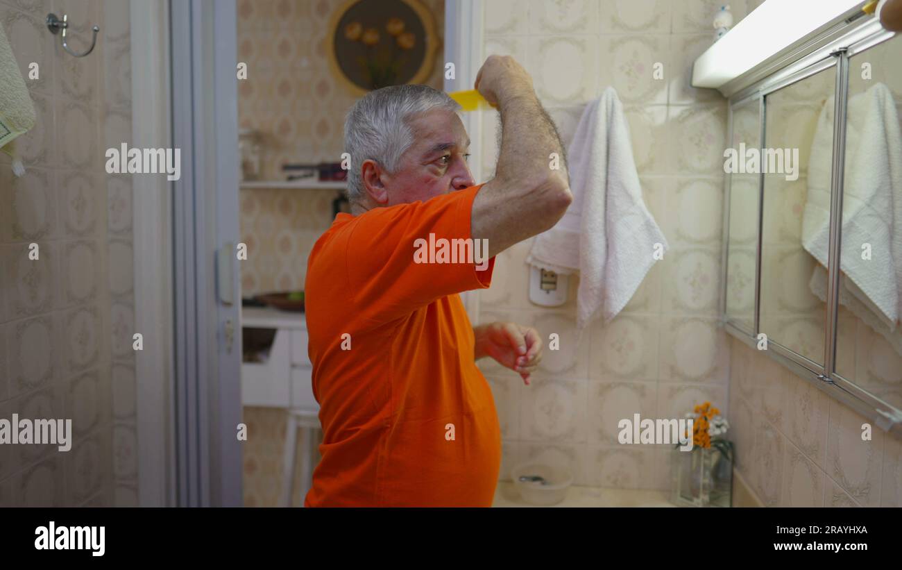 Senior man combing hair in front of bathroom mirror, domestic old age ...