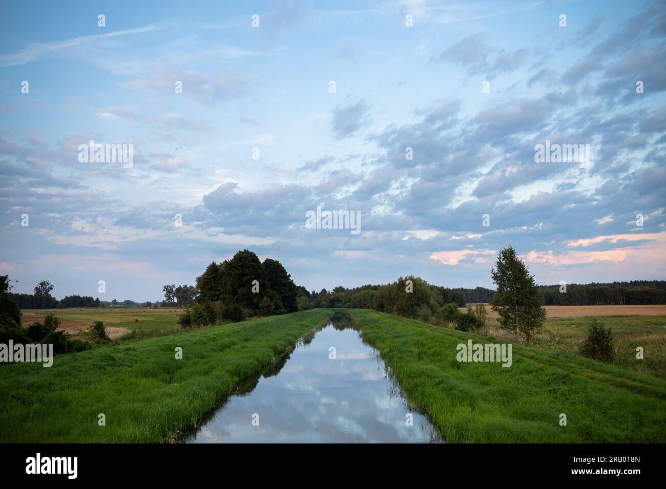 A slow-flowing wide river among lush green grasses and agricultural ...