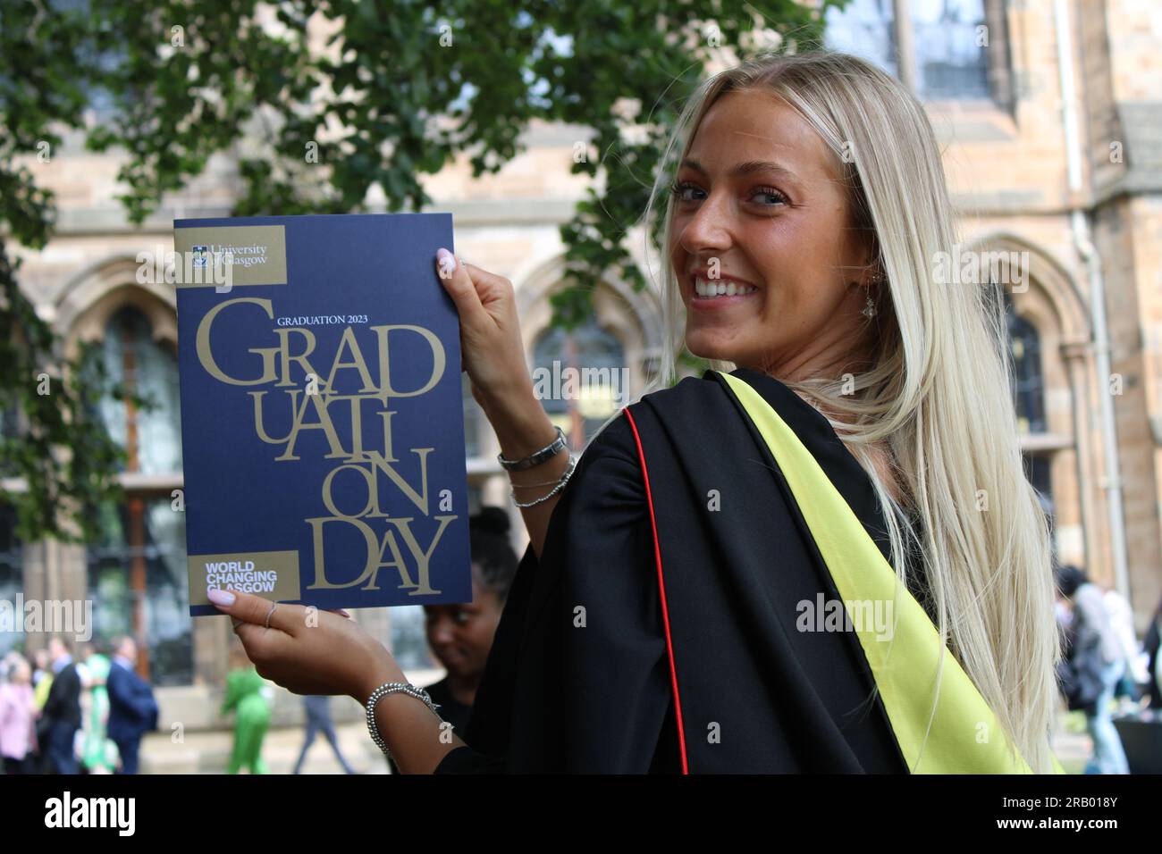 Smiling female student with long blonde hair wearing graduation gown ...