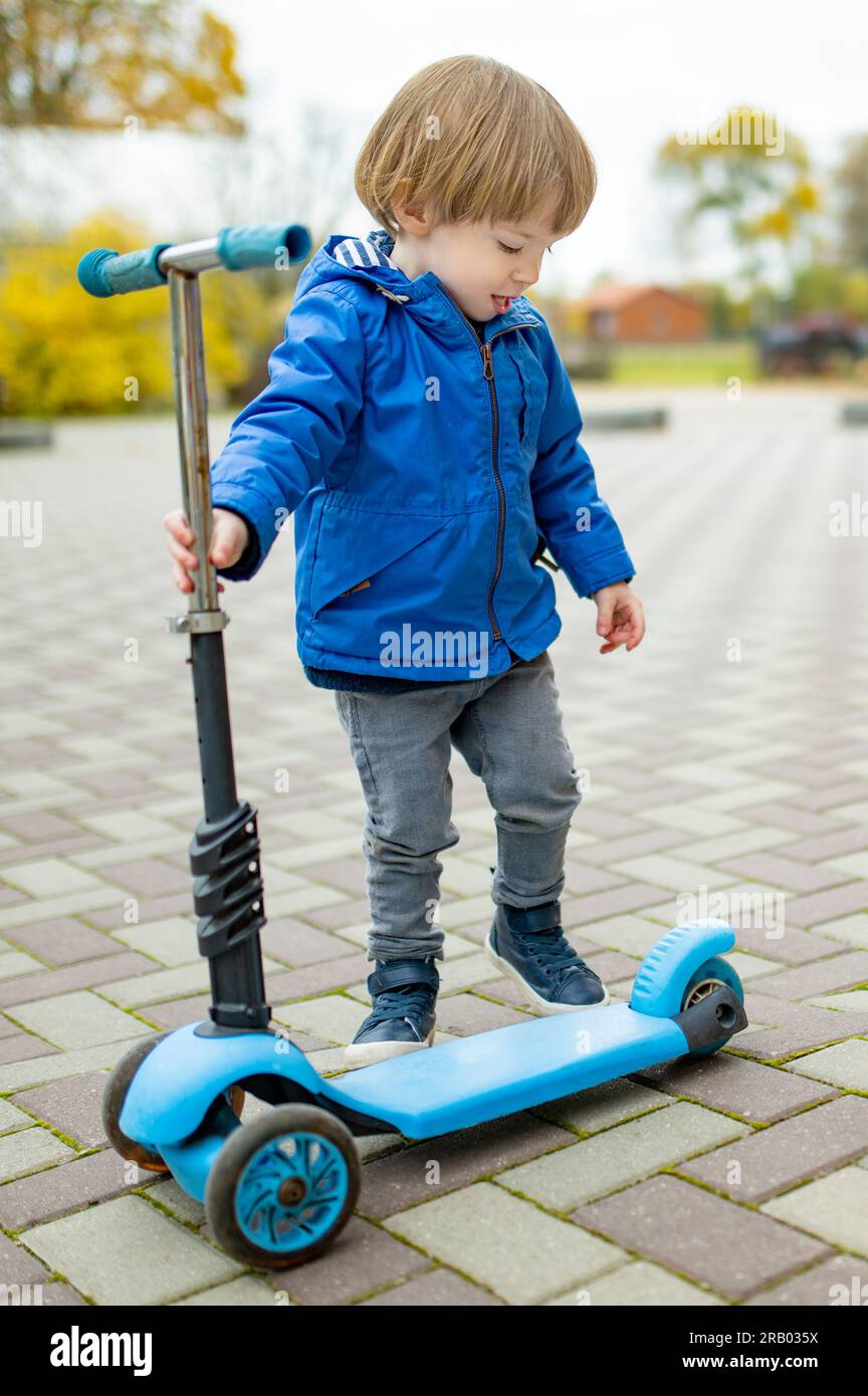 Adorable toddler boy riding his scooter in a city on sunny autumn ...