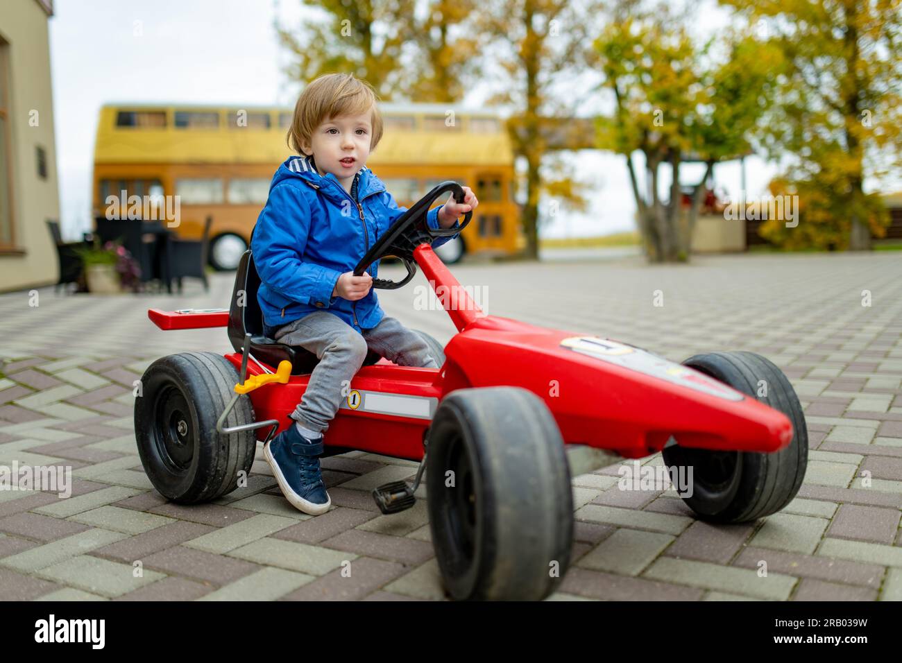 Adorable toddler boy riding his toy race car in a city on sunny autumn ...
