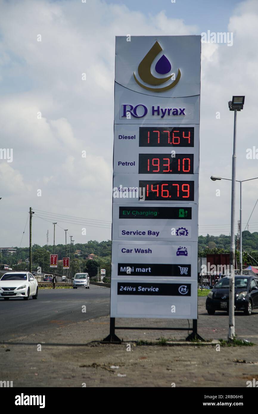 Motor vehicles, drive past a display board at a petro station showing ...