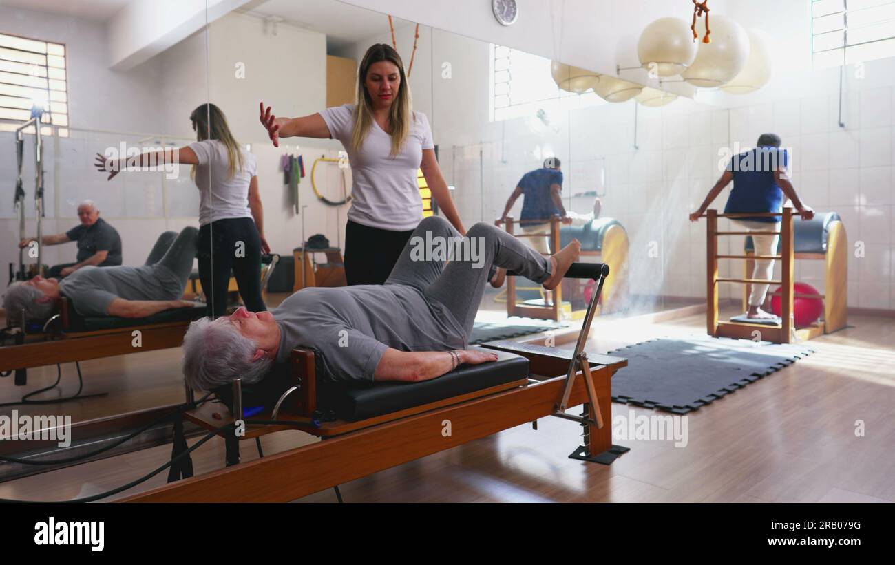 Female Pilates Instructor coaching Elderly Woman to use Machine. Old ...