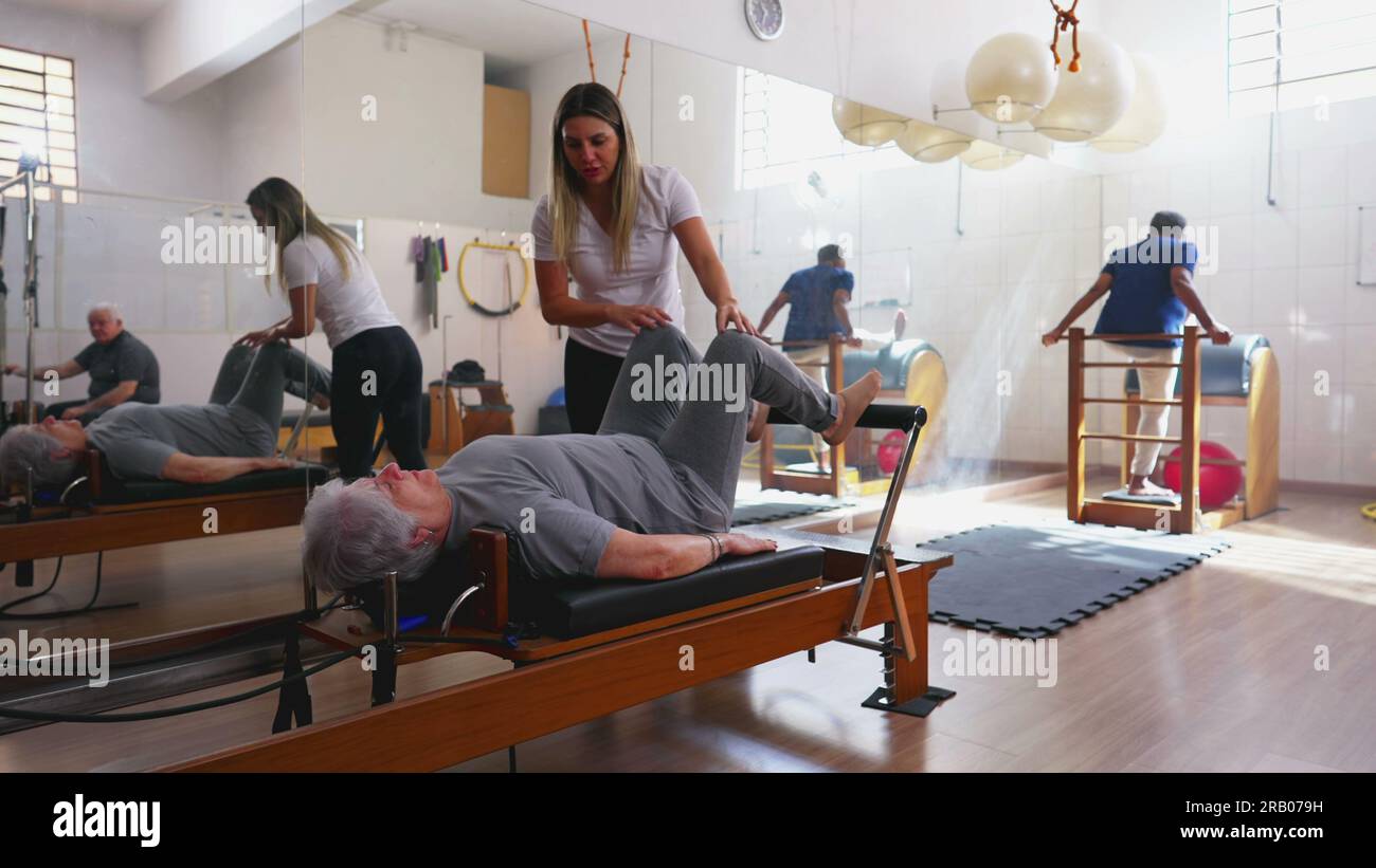 Female Pilates Instructor coaching Elderly Woman to use Machine. Old ...