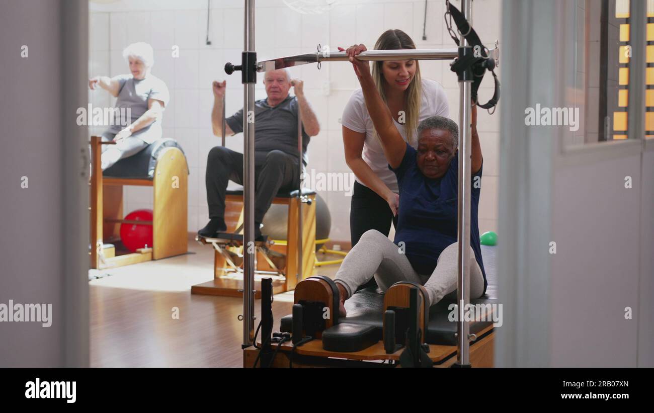Female Pilates coach assisting a senior black woman in group class ...