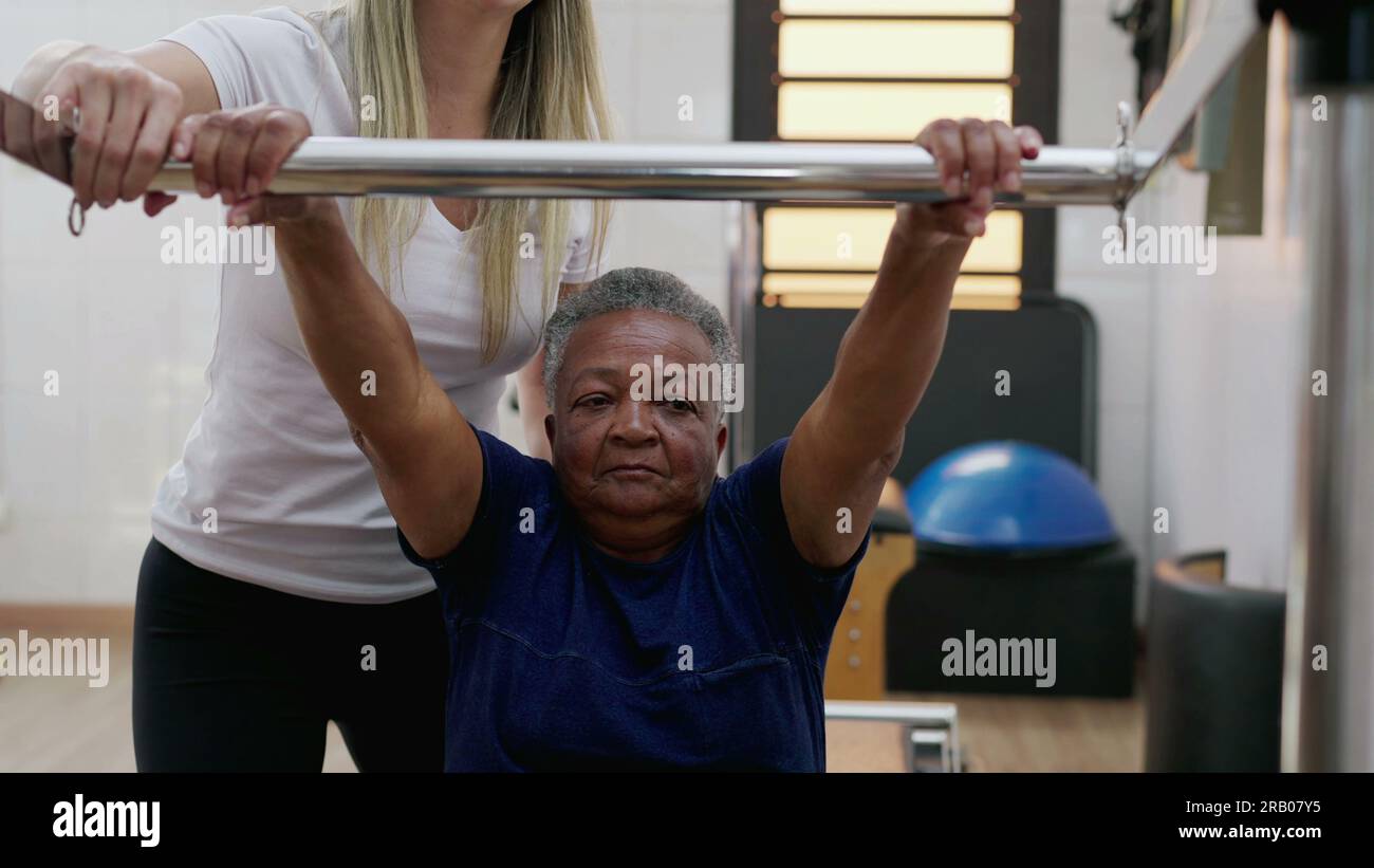 Female Pilates Coach assisting a black senior woman to use machine, old ...
