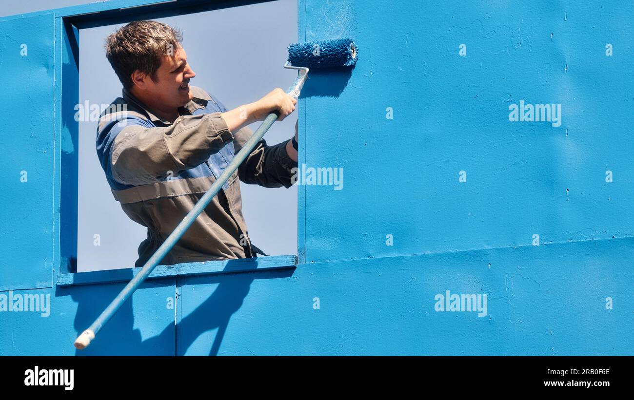 Professional painter in overalls paints metal wall of building with ...