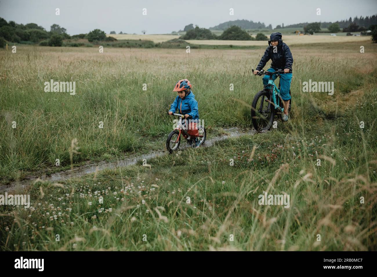 Mother and son riding bike across meadow in rain Stock Photo - Alamy