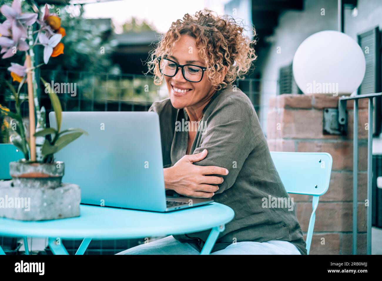 Happy woman using computer for video call outside home in the garden ...