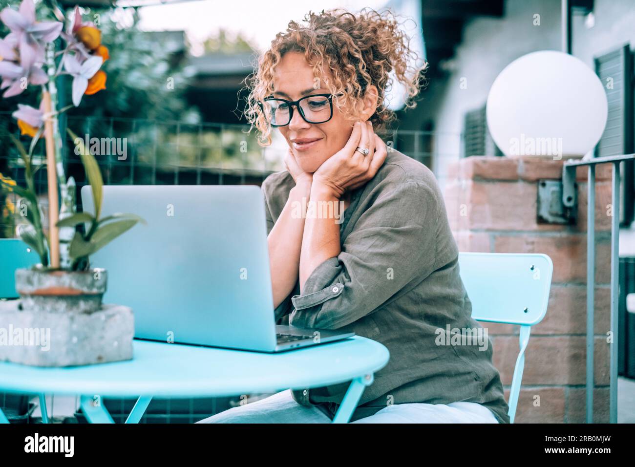 Serene woman using computer outdoor home at the table enjoying outdoor ...