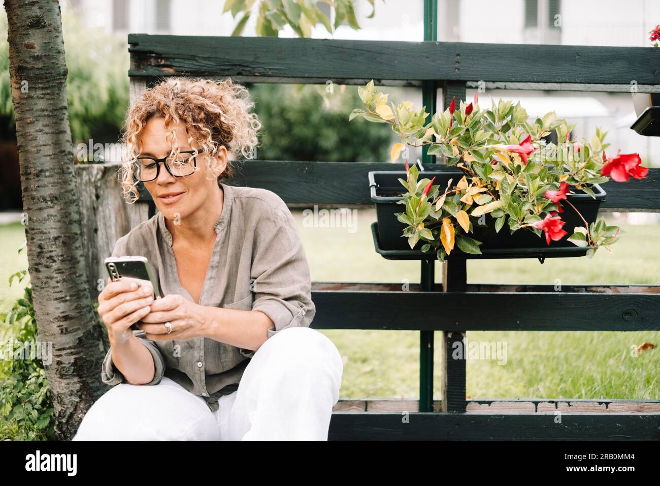 Pretty woman using cellphone mobile phone outdoor sitting in the garden ...