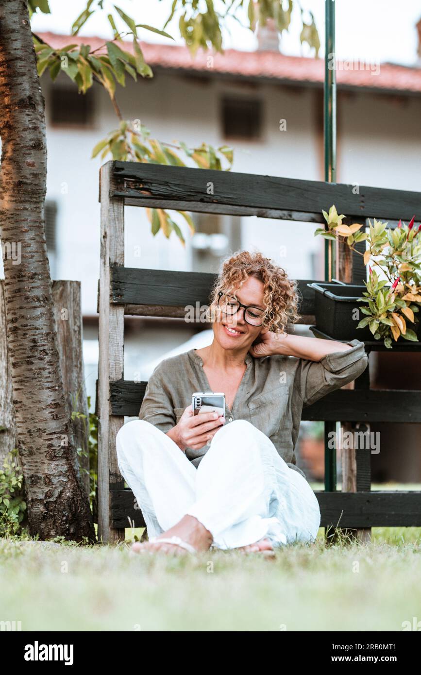 One cheerful adult woman enjoying mobile phone in the garden with house ...
