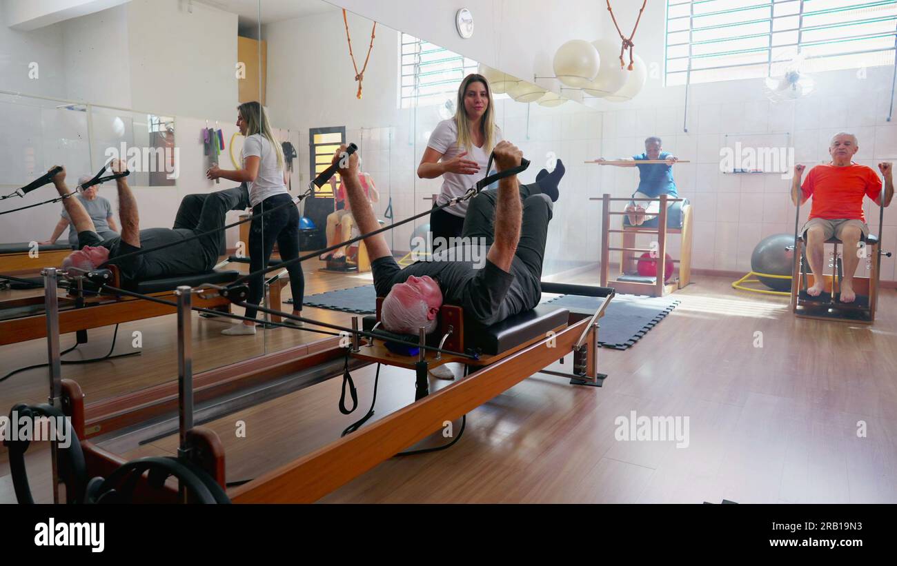 Pilates group session of elderly people exercising. Coach orienting a ...