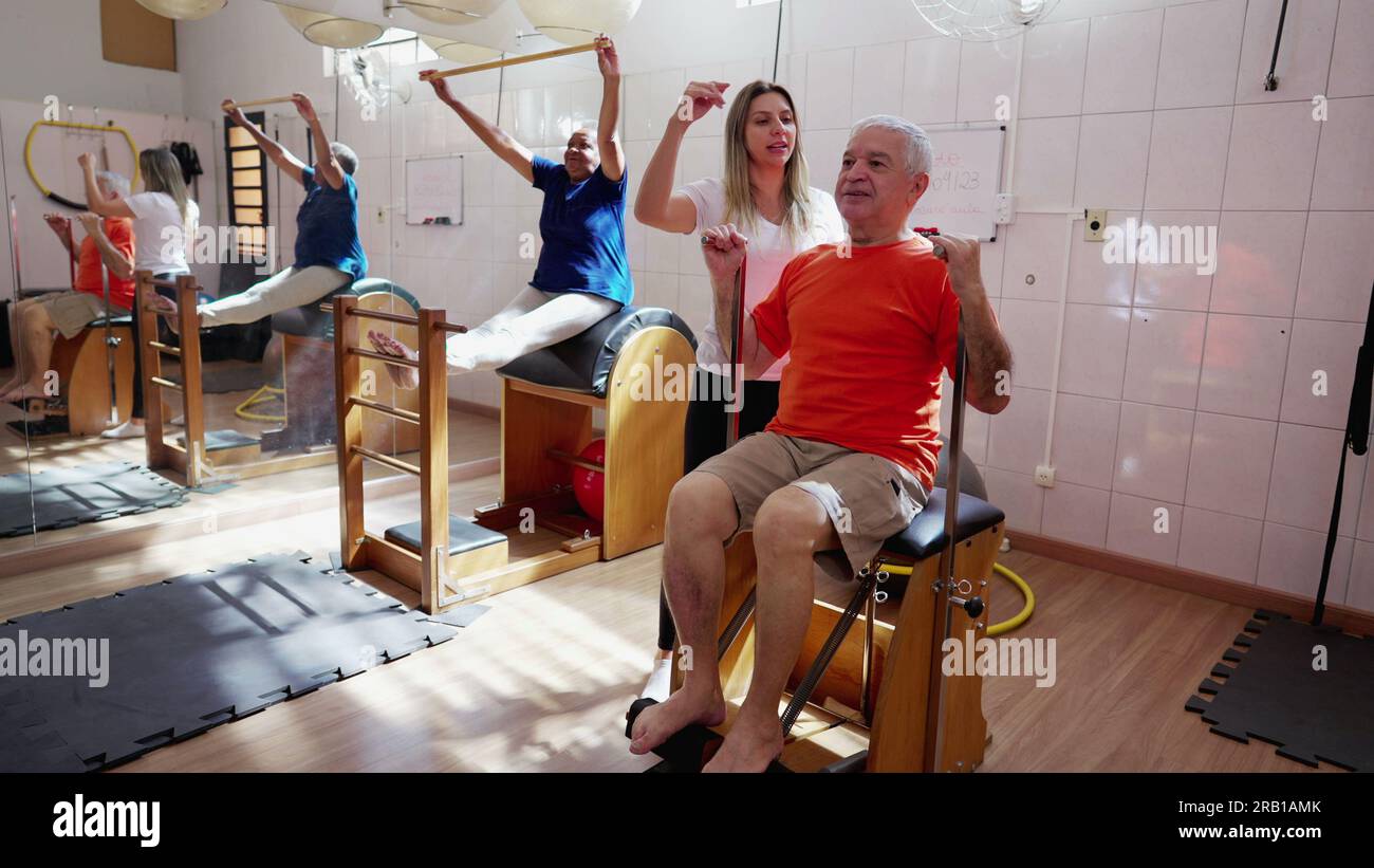 Pilates teacher coaching senior man with machine. Group physiotherapy ...