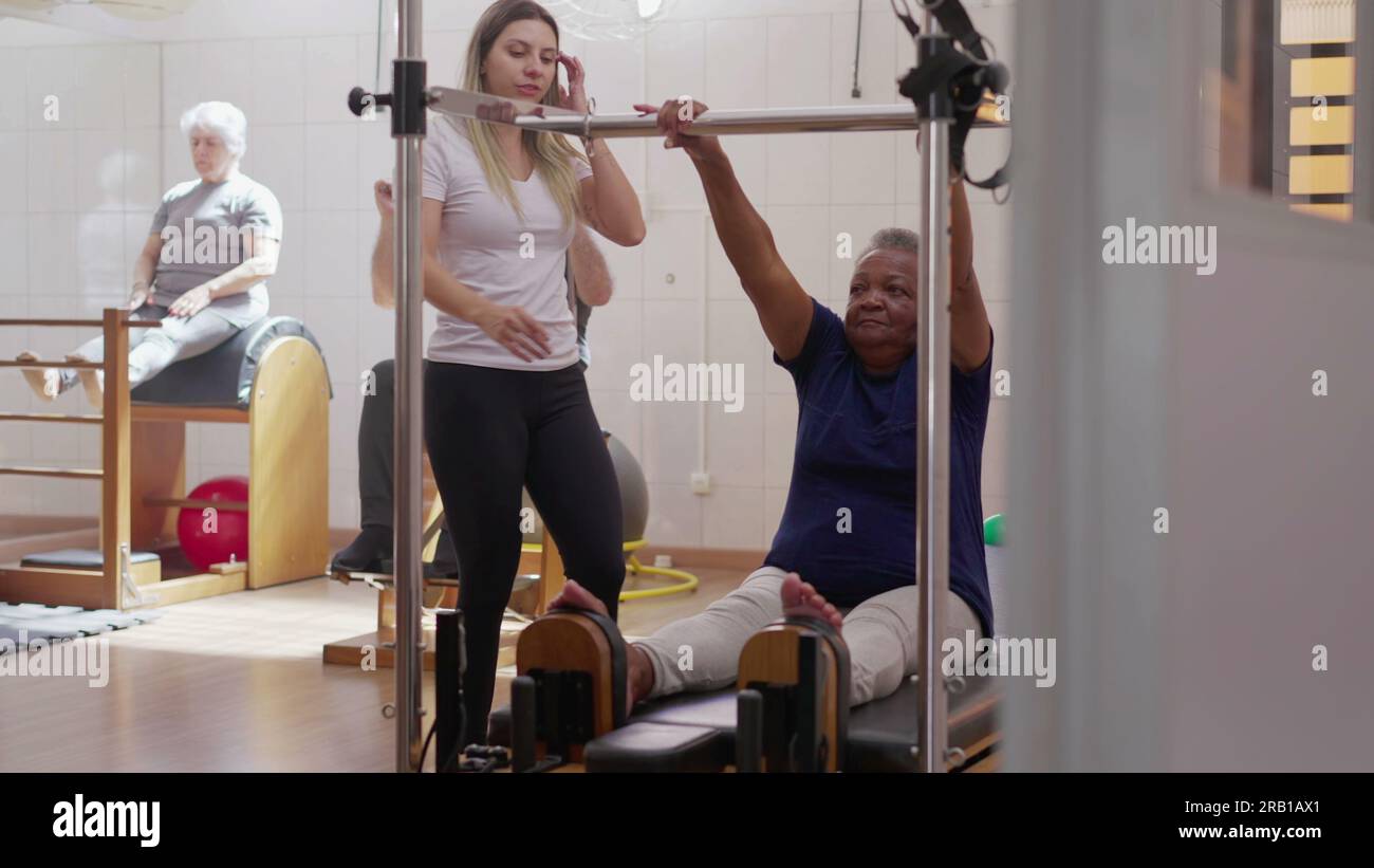 Senior exercising in Pilates Group Class, a black woman using machine ...