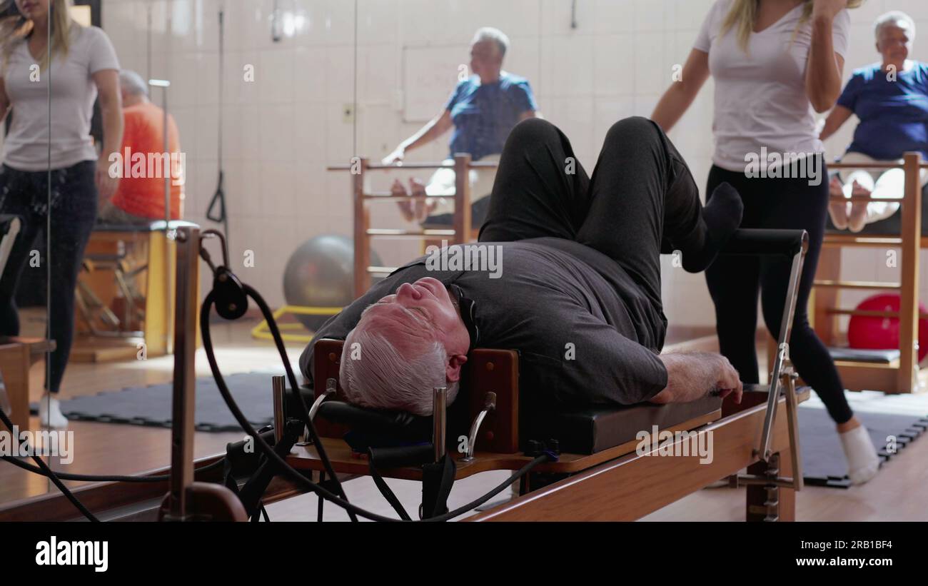 Pilates coach assisting senior man to use machine to strengthen body ...