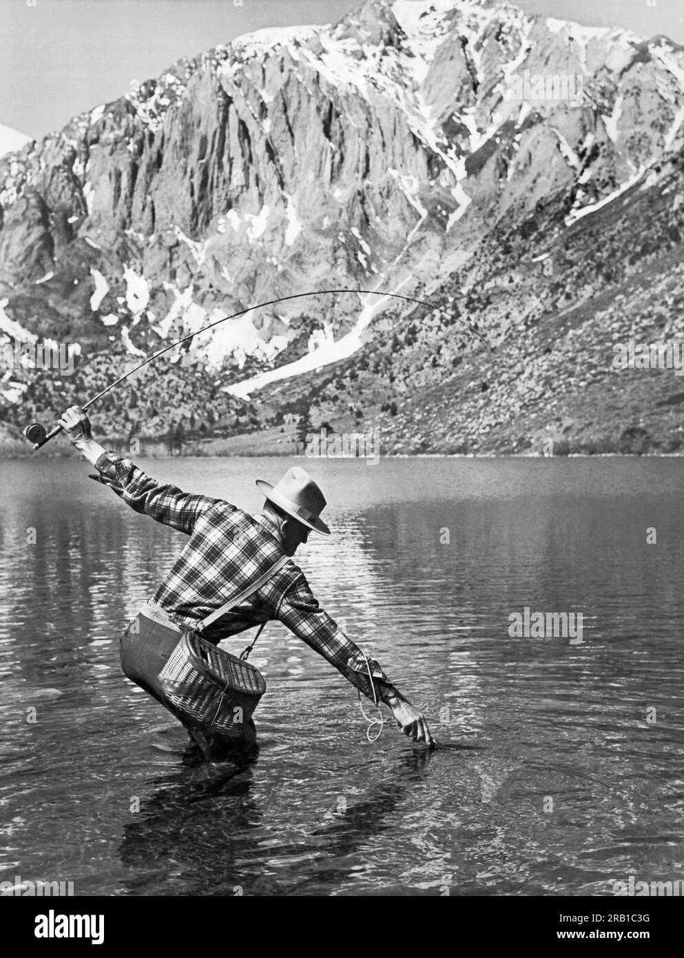 United States: c. 1950 A man fly fishing in a lake in the mountains ...