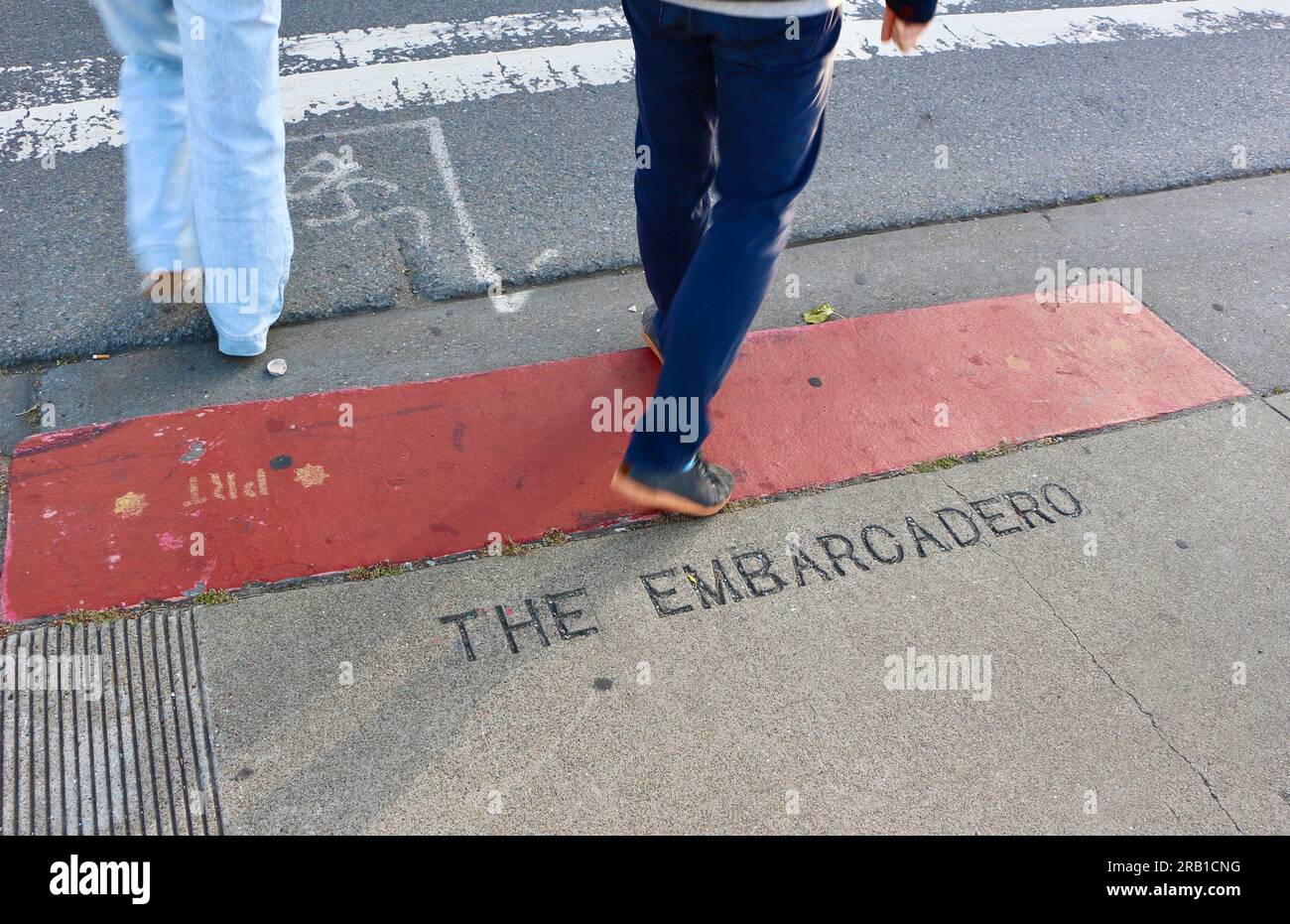 Pedestrians legs walking over a stamped sign in the concrete sidewalk ...