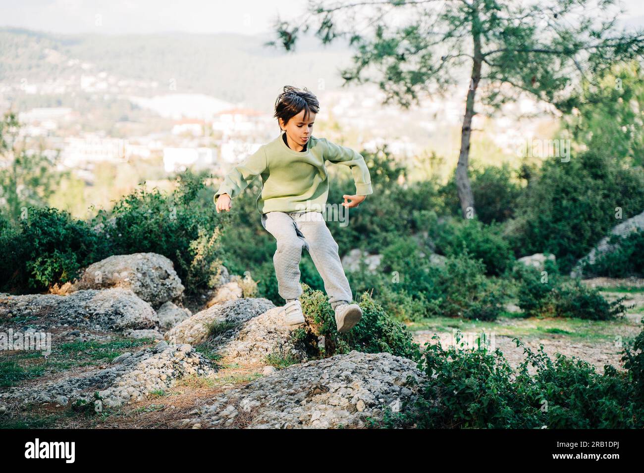 School kid child in vibrant clothes jumping over granite rock boulders ...