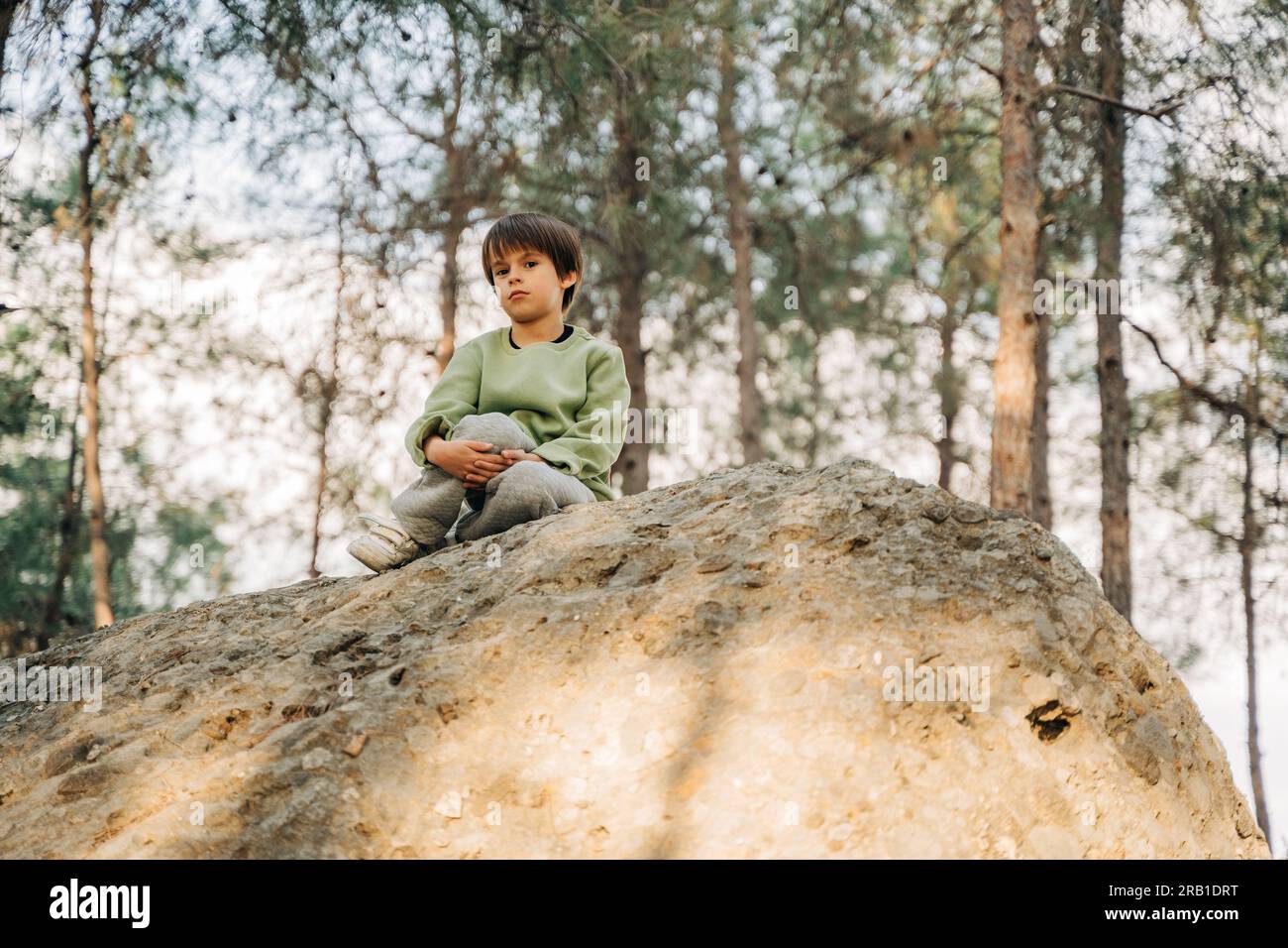 School kid boy child sitting on the granite rock boulder in the forest ...