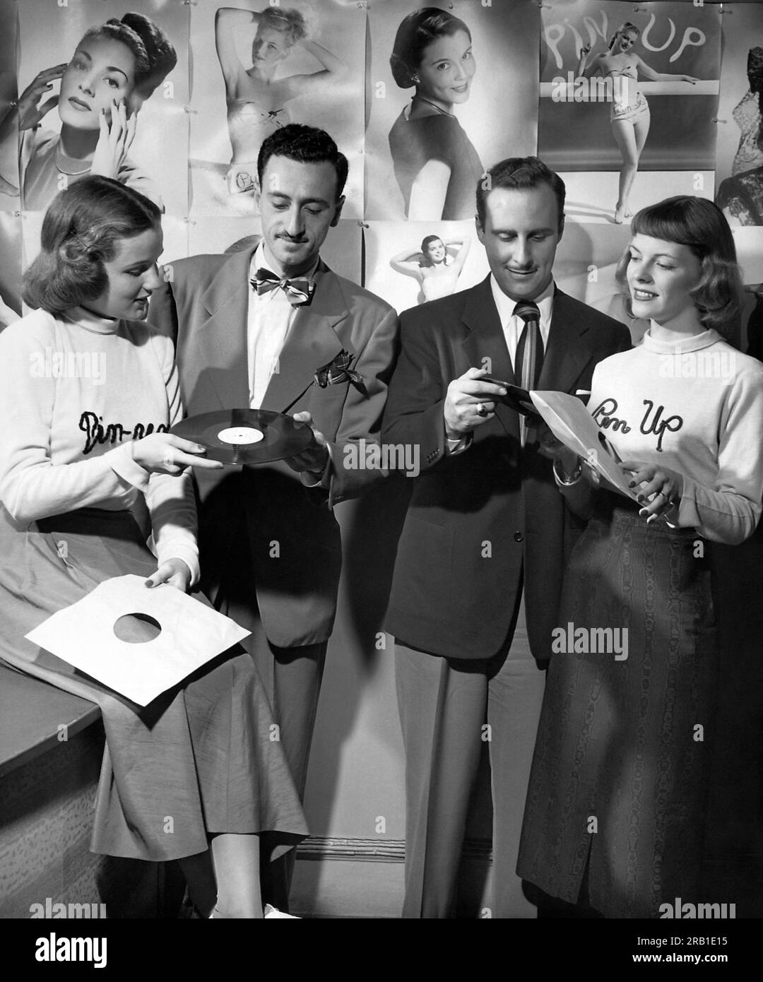 United States: c. 1958 Two men in suits look over LP records with two ...