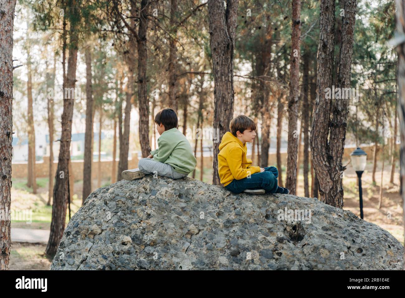 School kids boys having a conflict quarrel sitting on a rock boulder in ...
