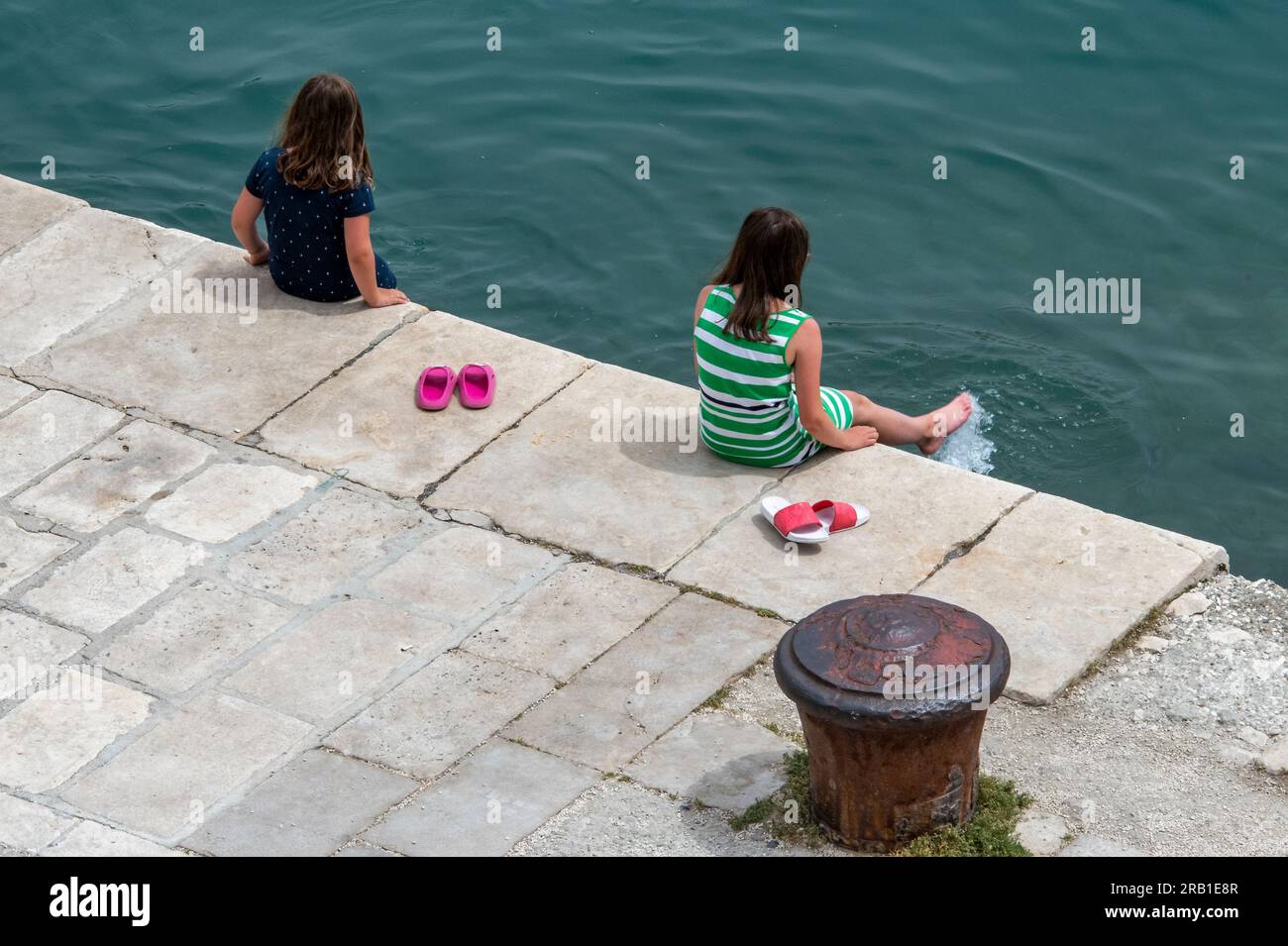 two young children sitting on a sea wall dipping feet in the water ...