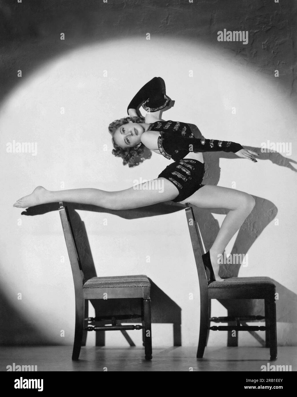 United States: c. 1927 A limber young woman stretches across two chairs ...