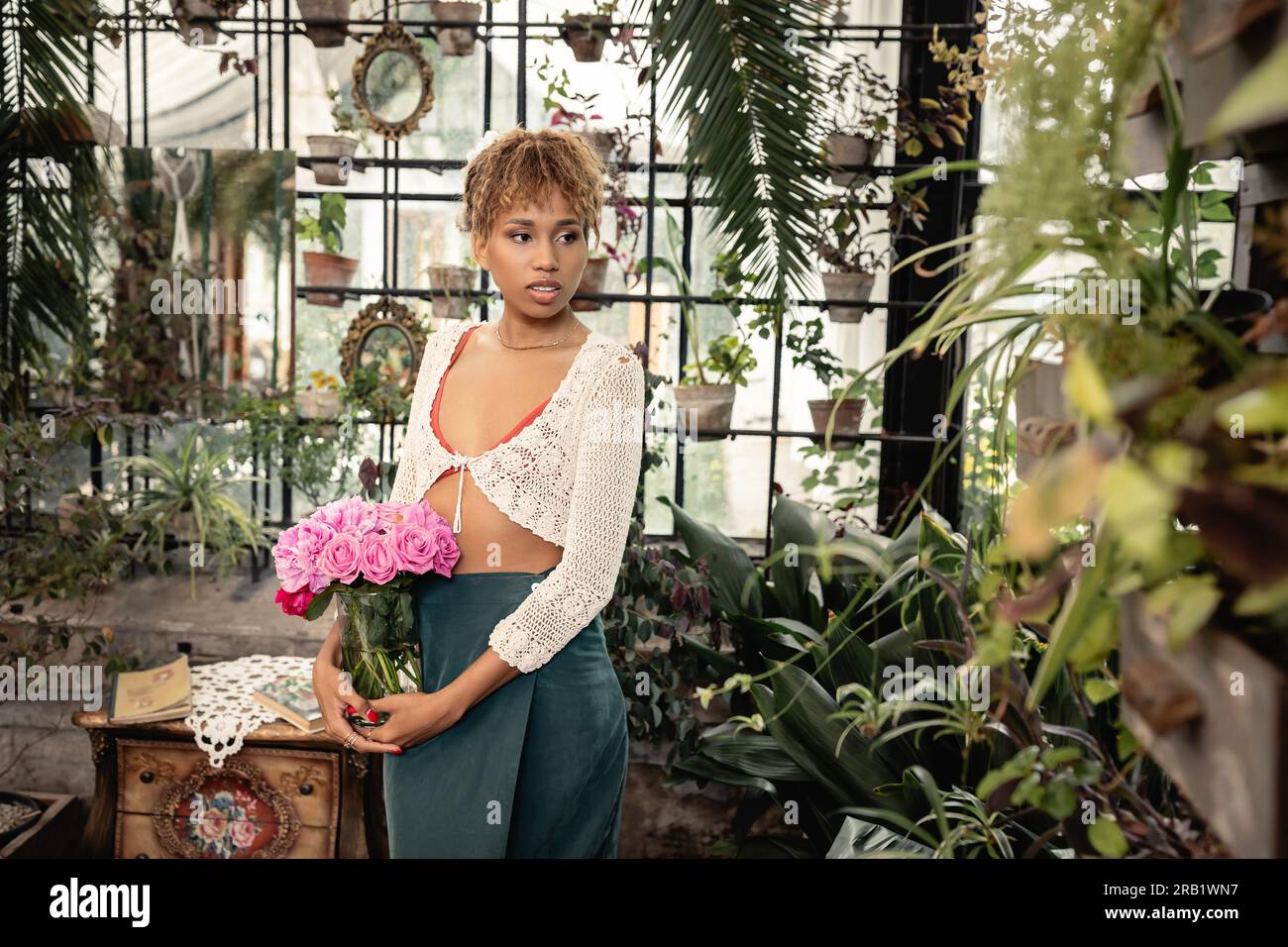 Young stylish african american woman in summer outfit holding vase with ...
