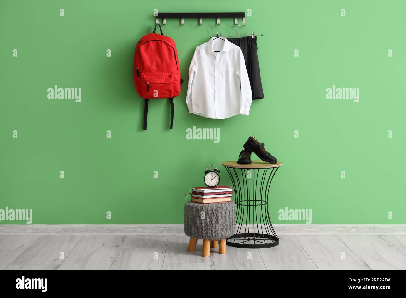 Rack with stylish school uniform, bench and table near green wall in ...