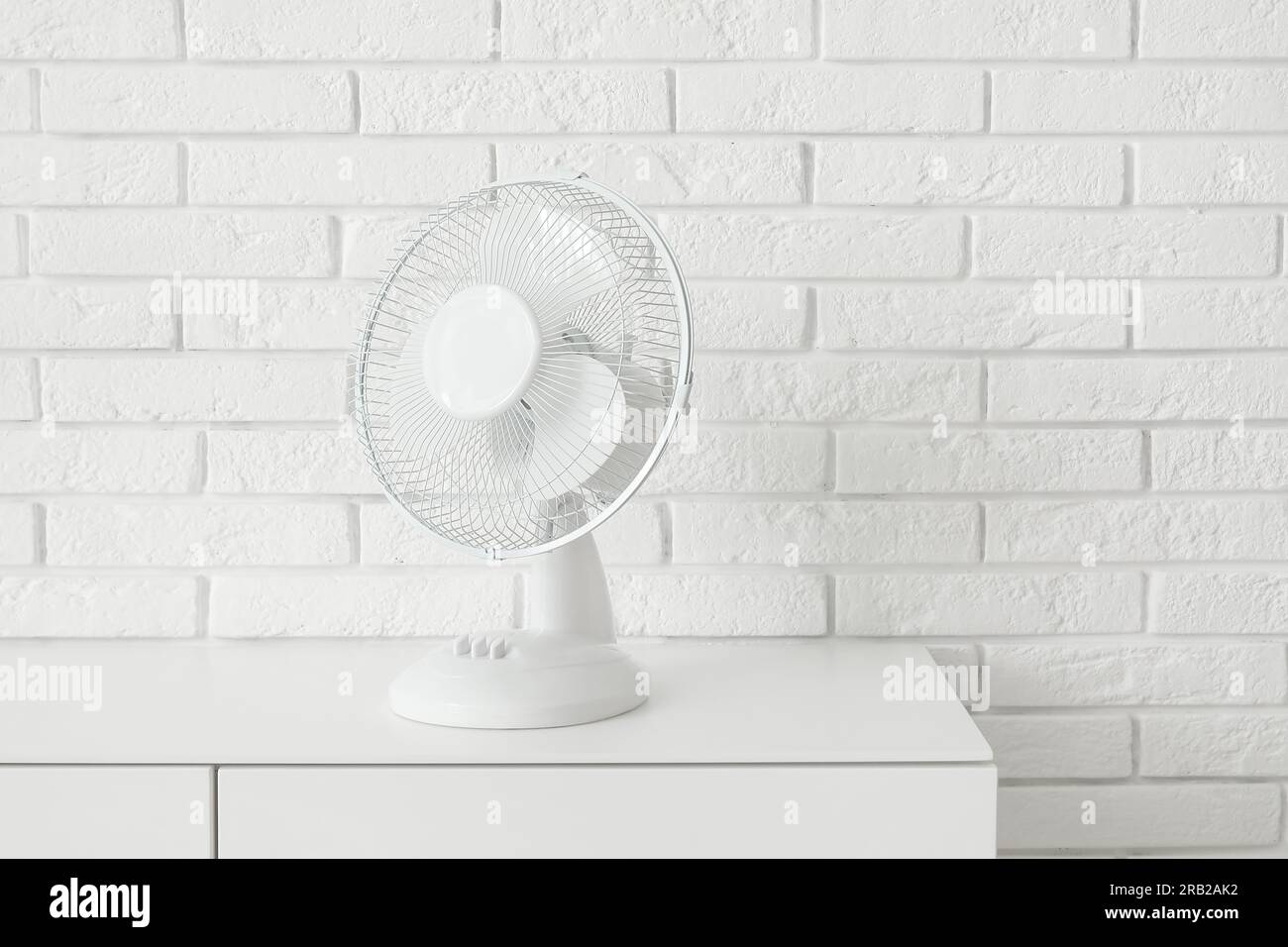 Stylish cabinet with modern electric fan near white brick wall Stock ...