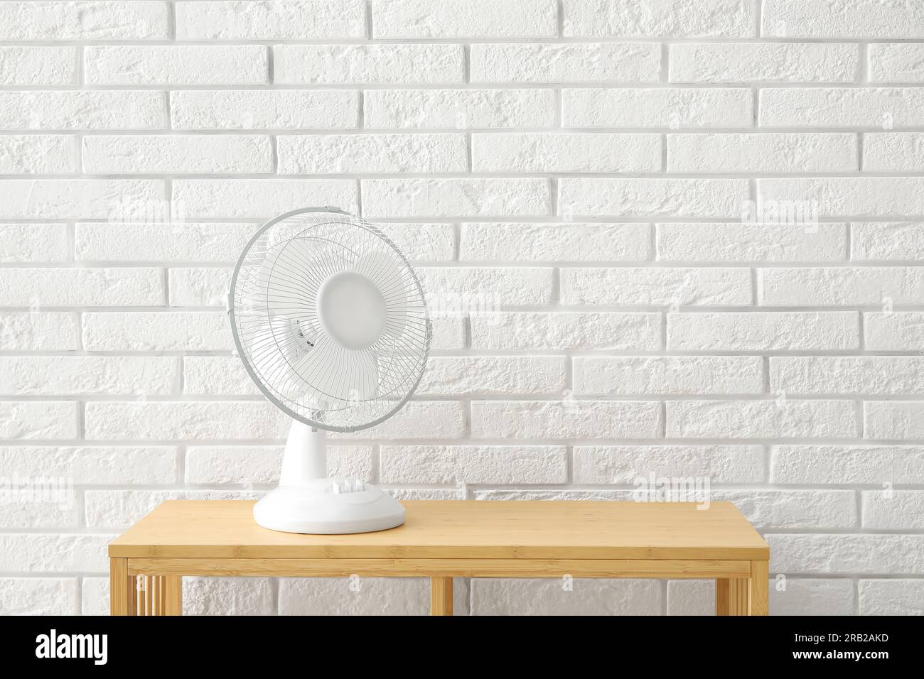 Wooden table with modern electric fan near white brick wall Stock Photo ...