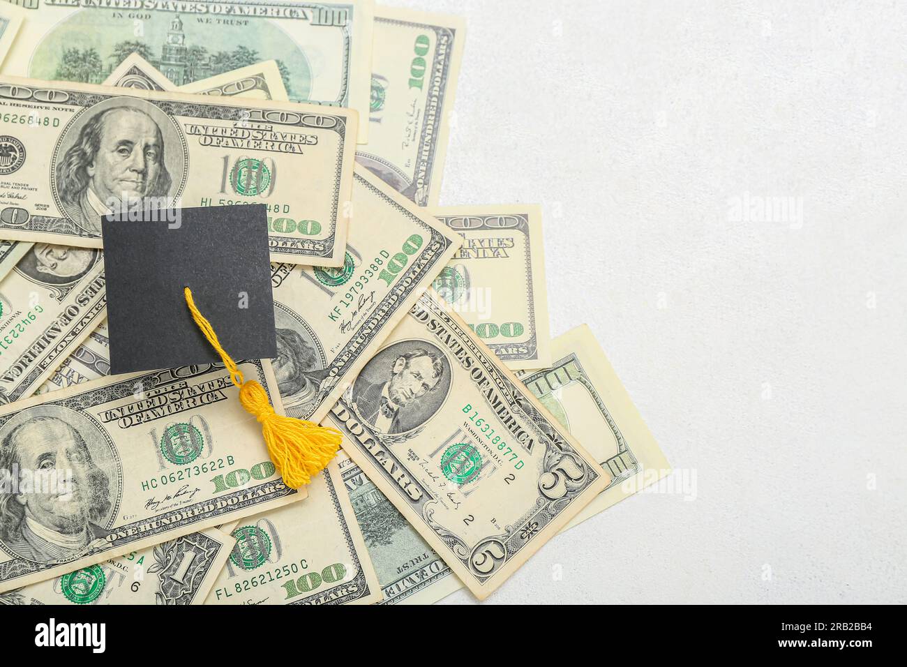 Graduation hat and pile of dollar banknotes on white background ...