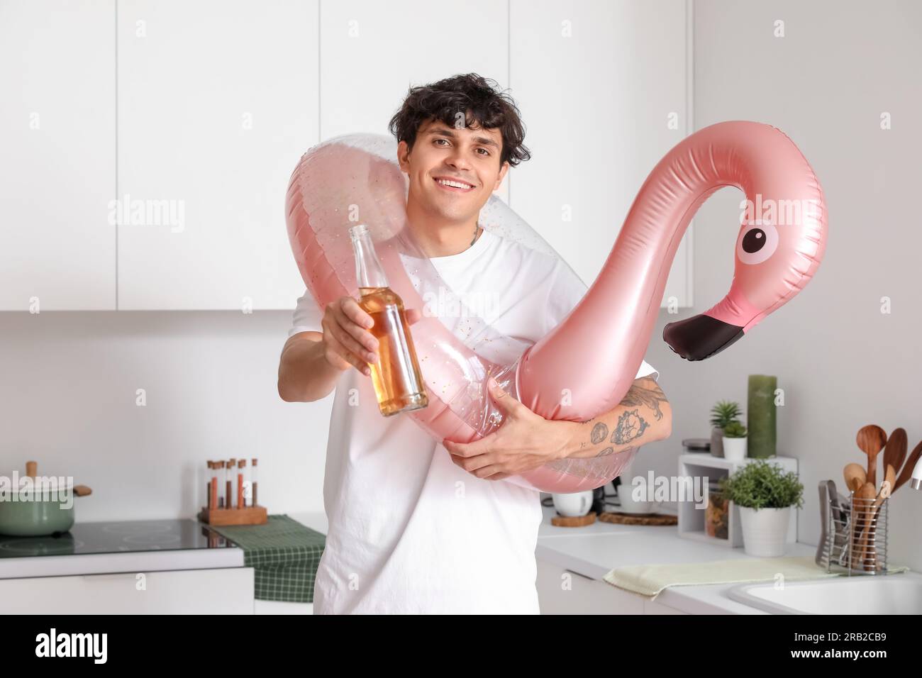 Young man with beer and swim ring ready for summer vacation in kitchen ...