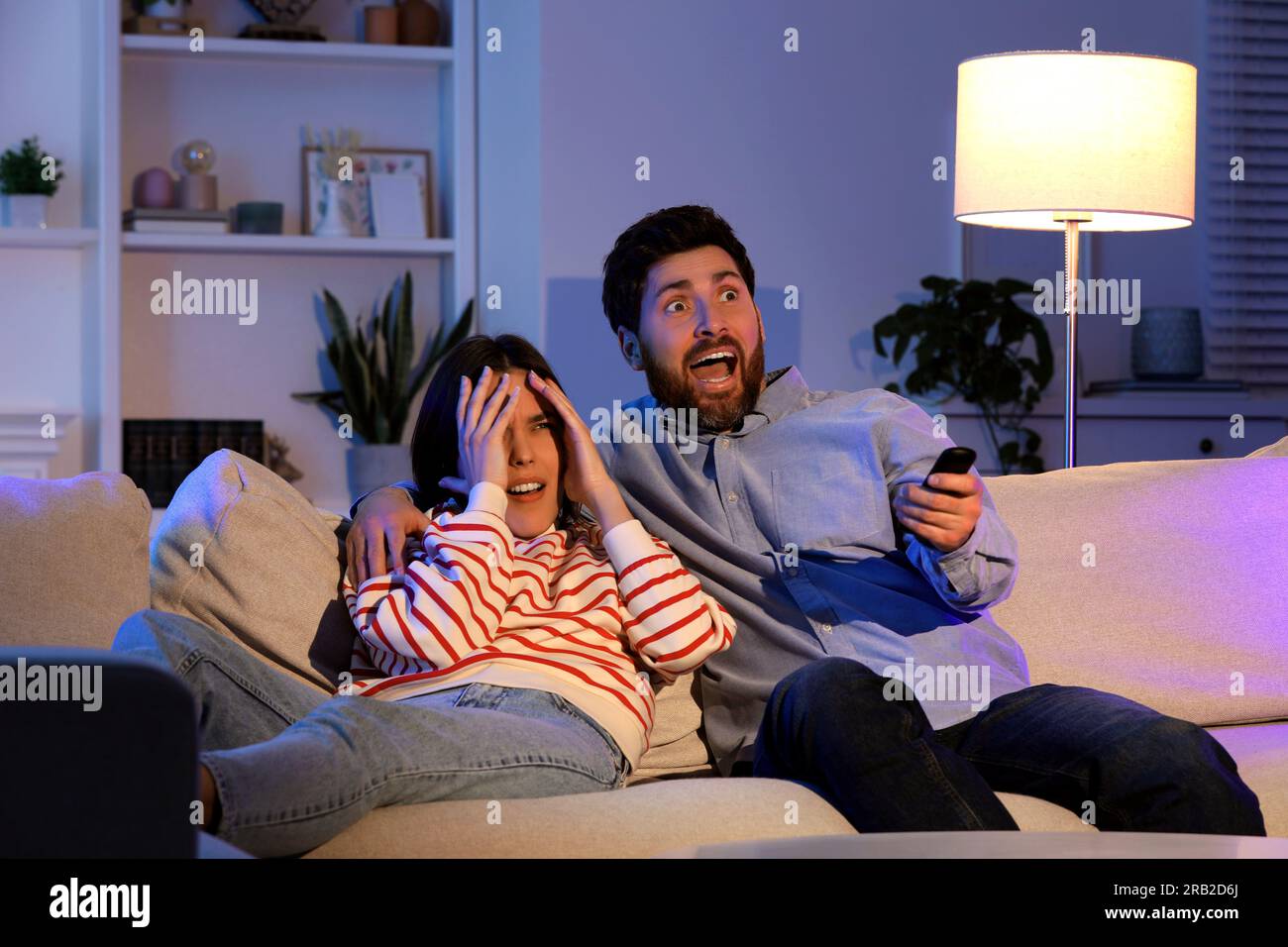 Frightened couple watching TV on sofa at home Stock Photo - Alamy