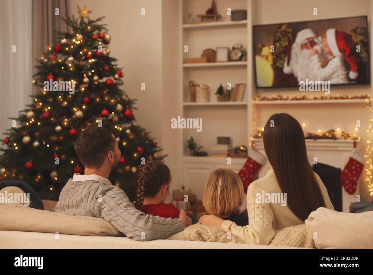 Family watching Christmas movie via TV in cosy room, back view. Winter ...