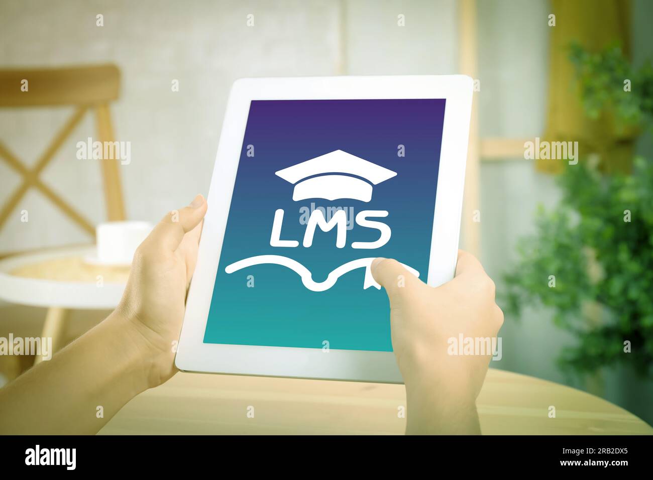 Learning management system. Woman using tablet at table, closeup. Open book and graduate cap ...