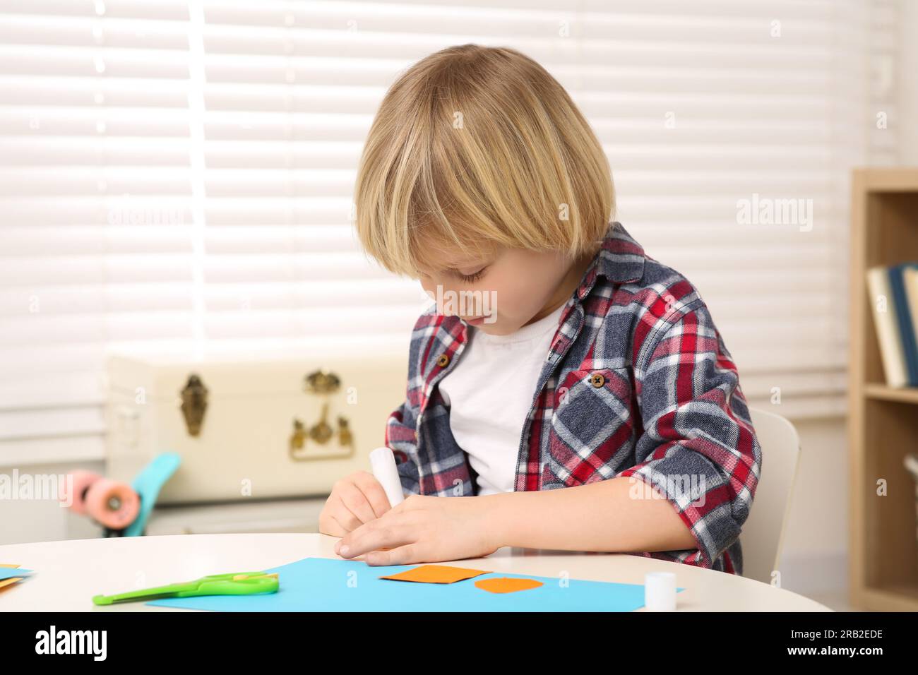 Cute little boy using glue stick at desk in room. Home workplace Stock ...
