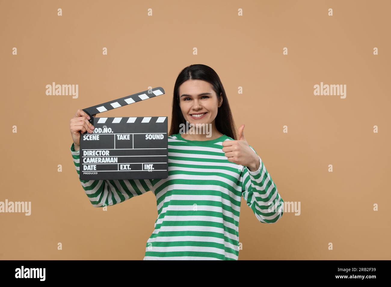 Happy actress with clapperboard showing thumbs up on beige background ...
